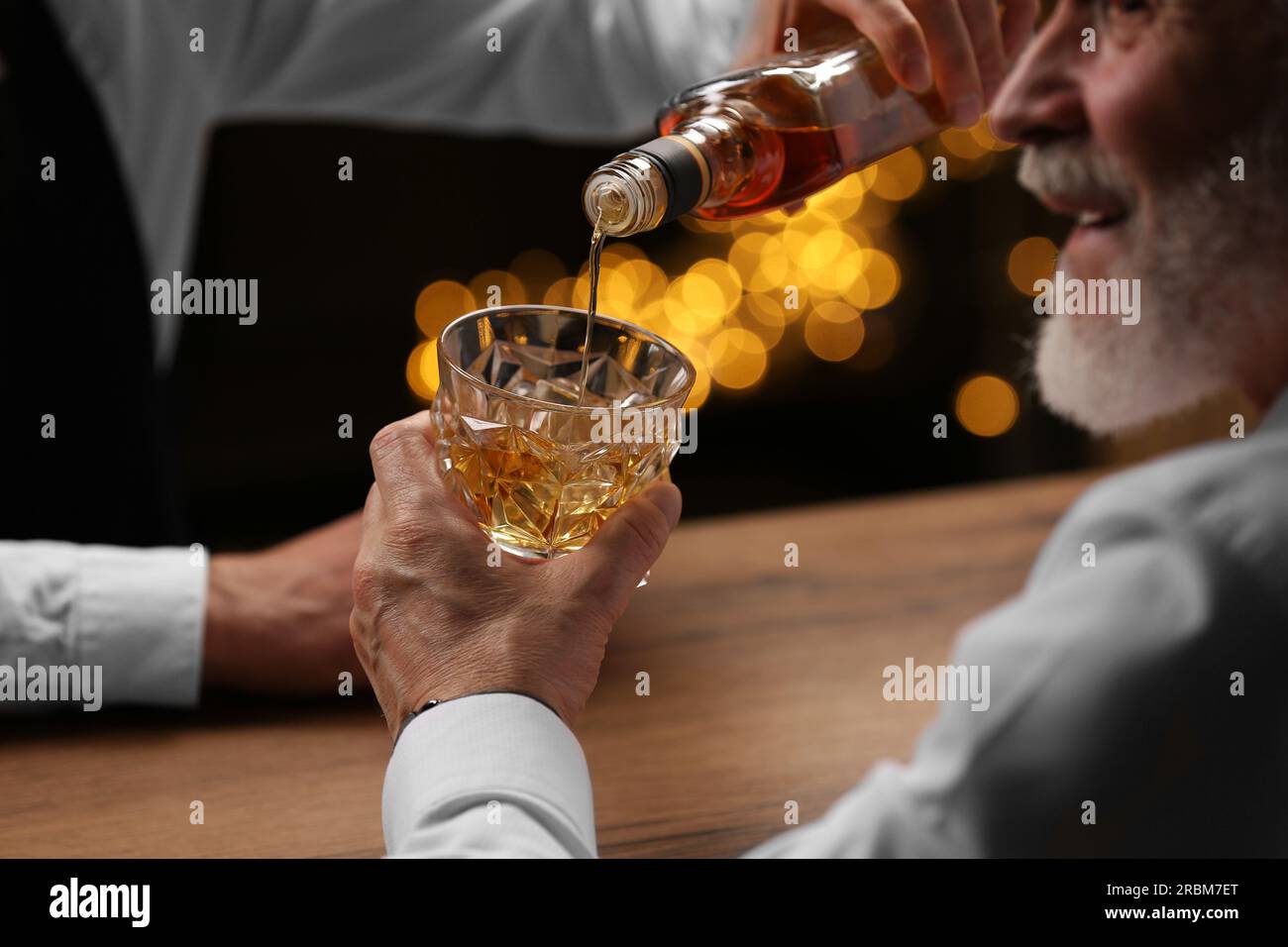 Bartender pouring whiskey in glass for customer at bar counter, closeup ...