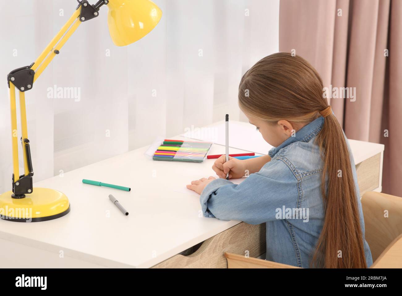 Cute little girl drawing with markers at desk in room. Home workplace ...