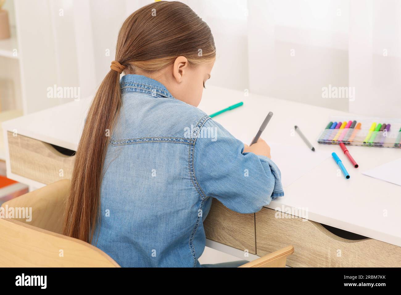 Cute little girl drawing with marker at desk in room. Home workplace ...