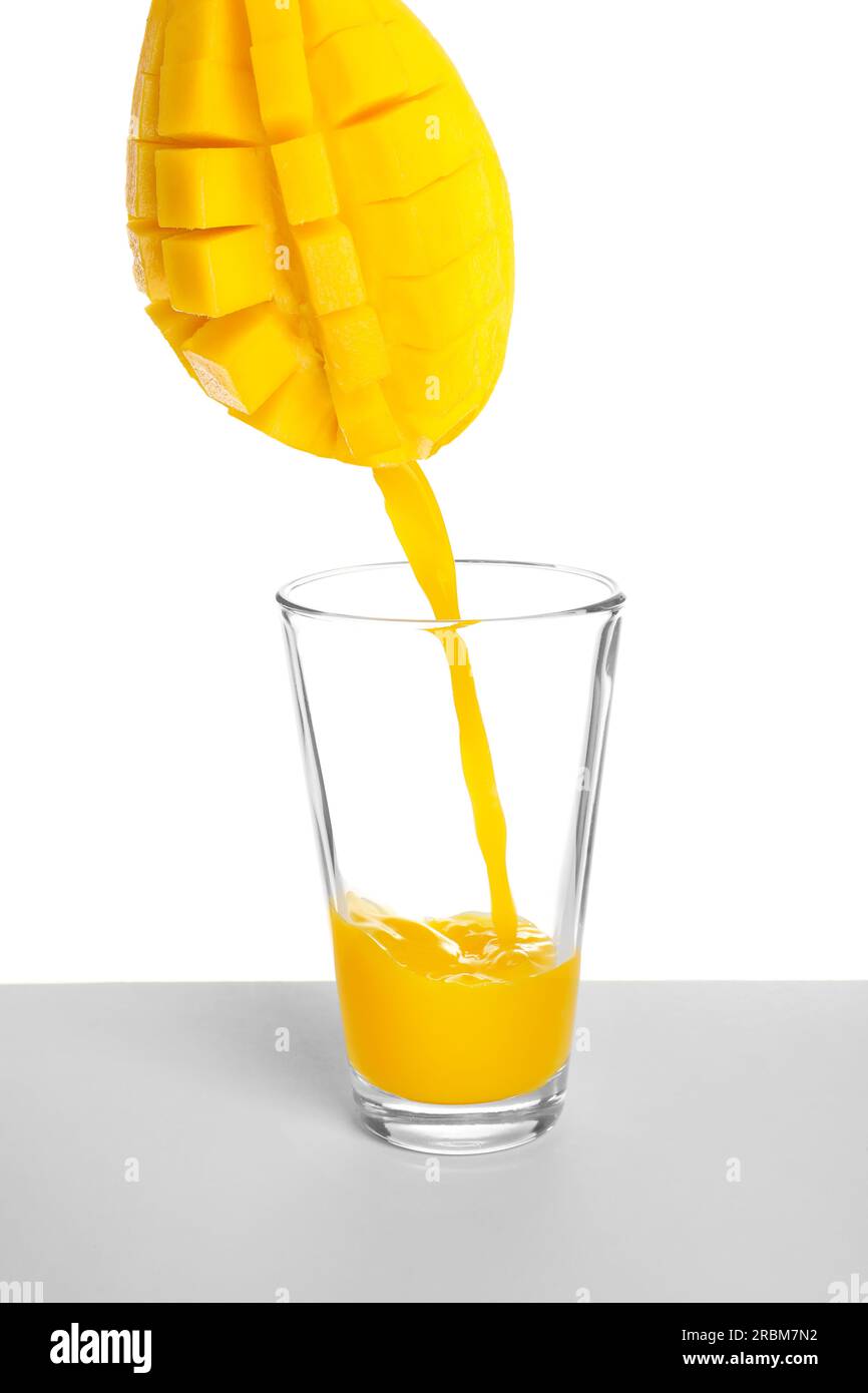 Making mango fresh. Juice pouring from mango into glass on white ...