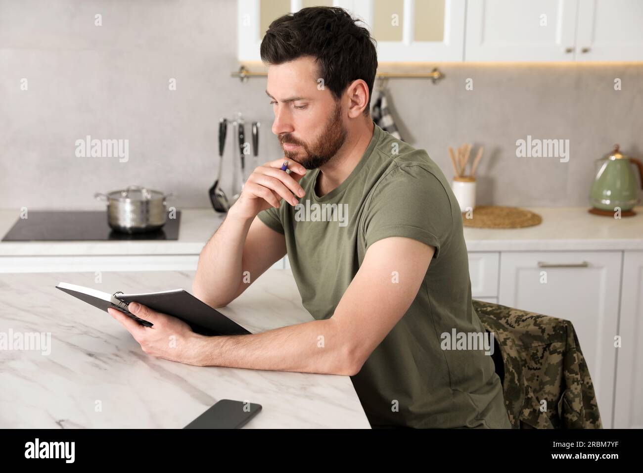 Soldier with notebook at white marble table in kitchen. Military ...