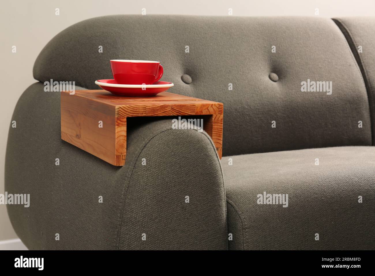 Cup of tea on sofa with wooden armrest table in room. Interior element ...