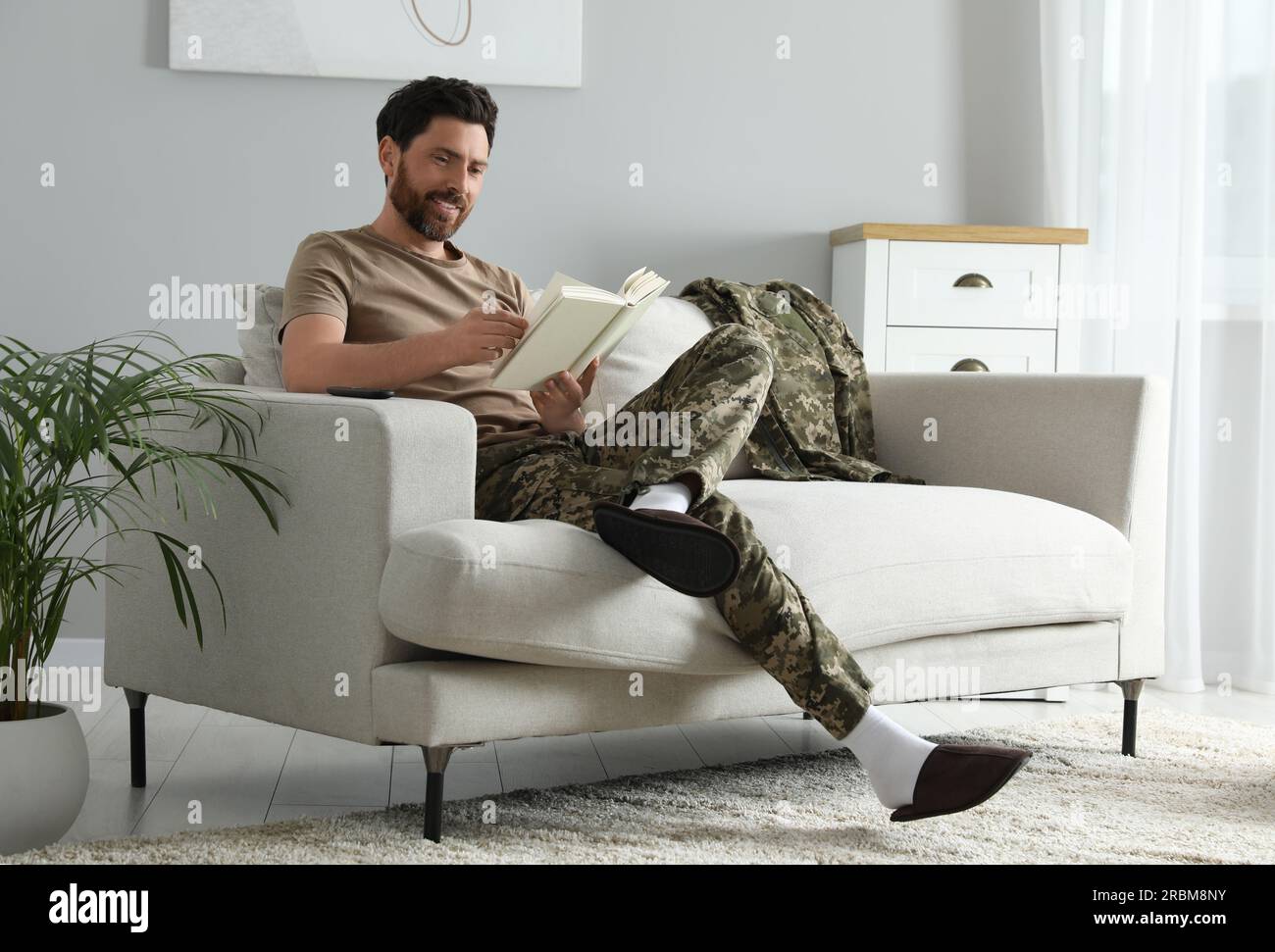 Happy soldier reading book on soft sofa in living room. Military ...