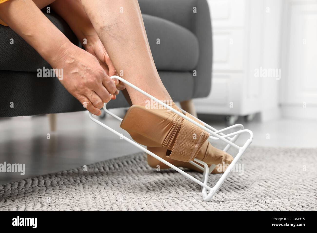 Woman putting on compression tights with stocking donner in living room ...