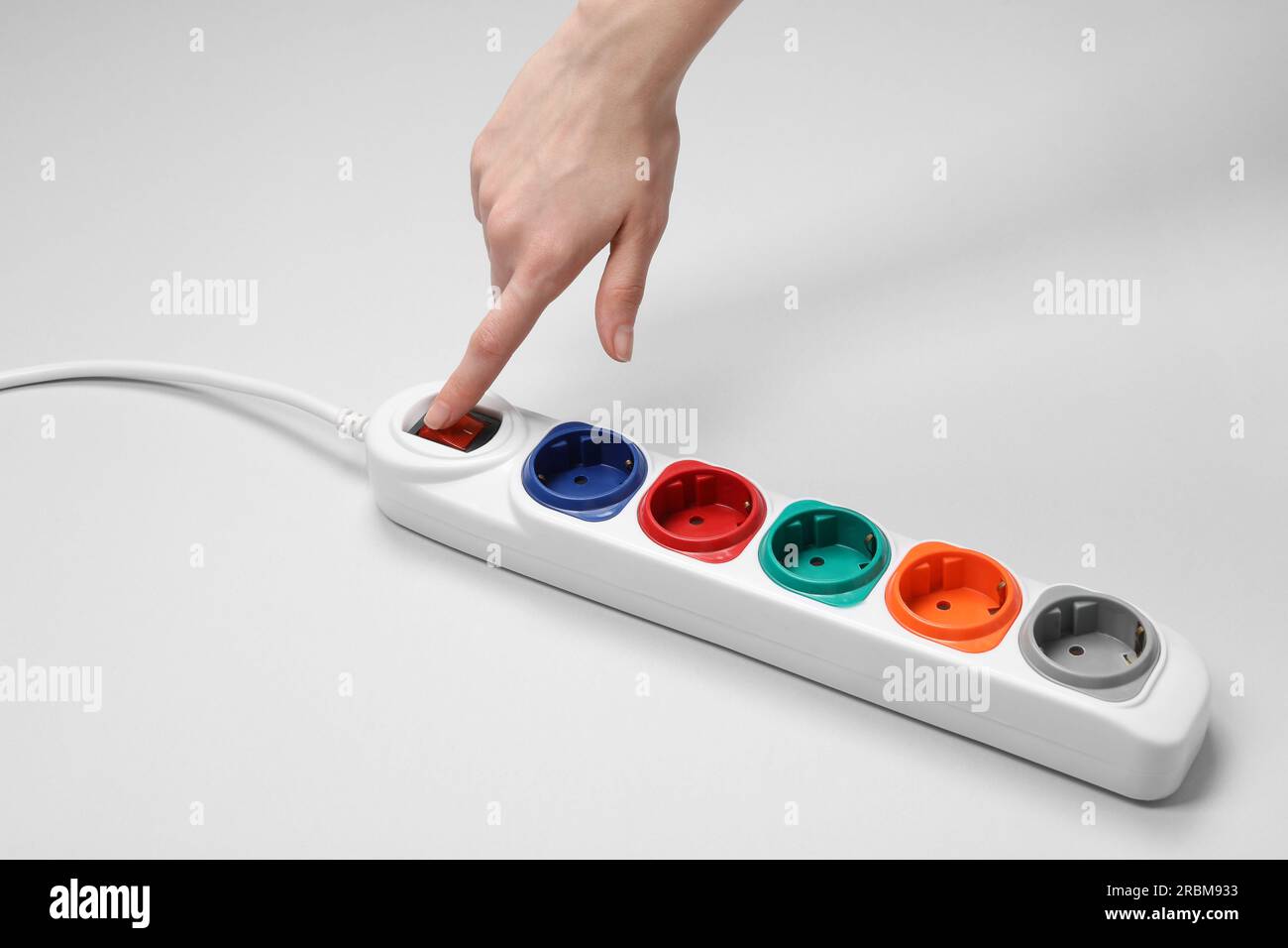 Woman pressing switch button of power strip on white background ...