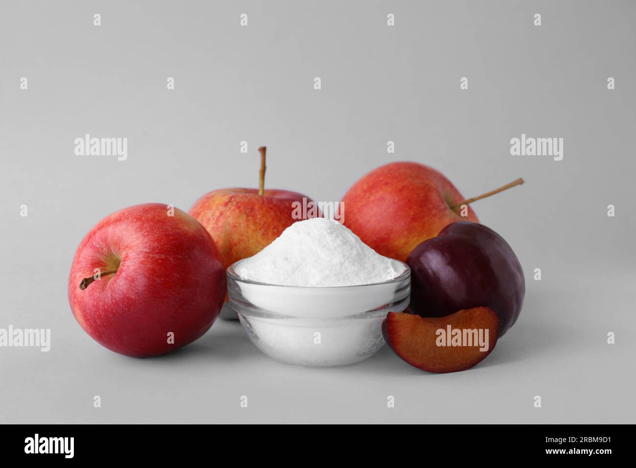 Bowl with sweet fructose powder, ripe apples and plums on white ...