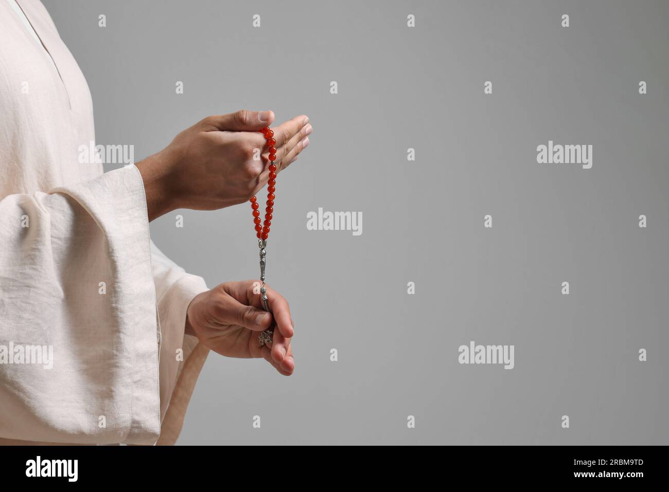 Muslim man with misbaha on light grey background, closeup. Space for ...