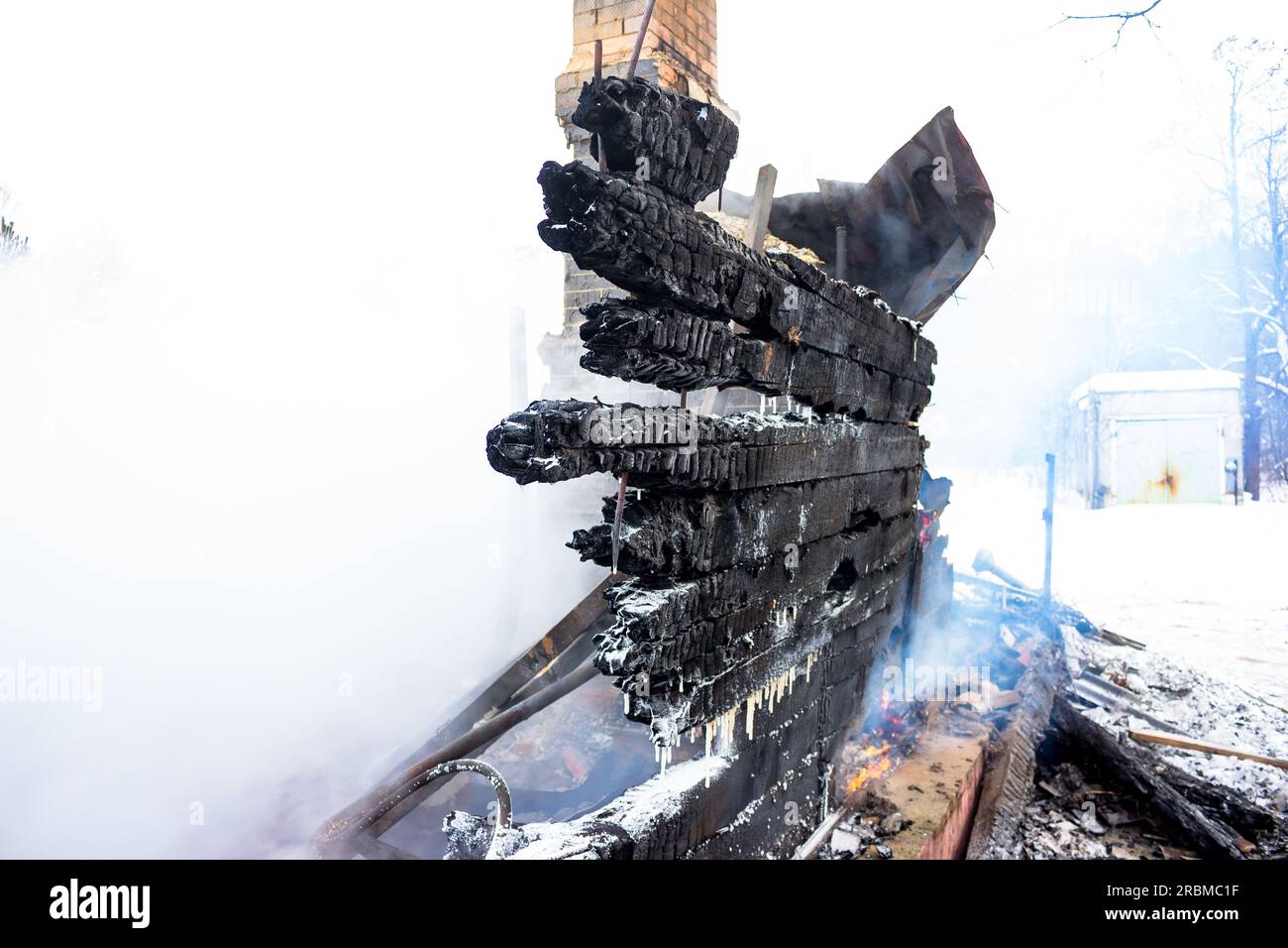 Charred planks and smoke on the ashes, burnt walls of a wooden house ...