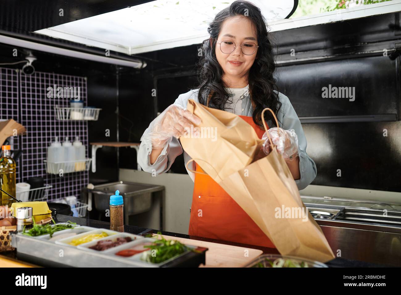 Smiling food truck worker putting packed sandwich in paper bag for ...