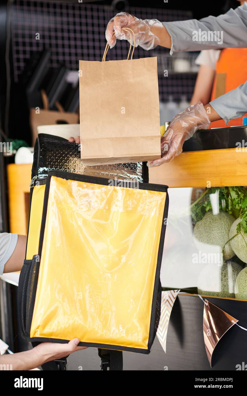 Food truck worker putting packed order in bag of delivery man Stock ...