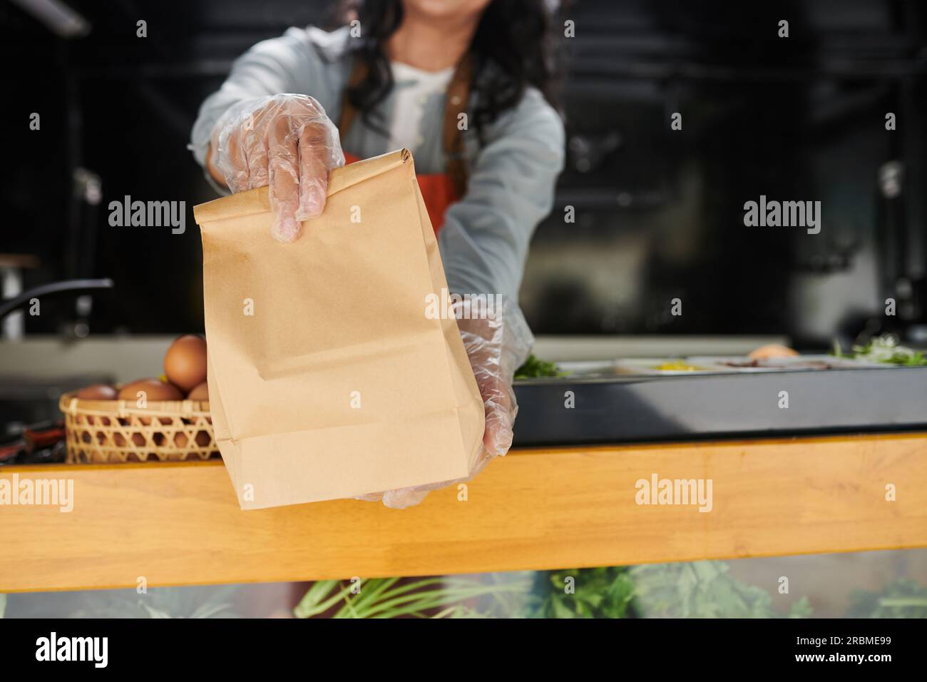 Food truck worker wearing gloves giving paper package with cooked order ...