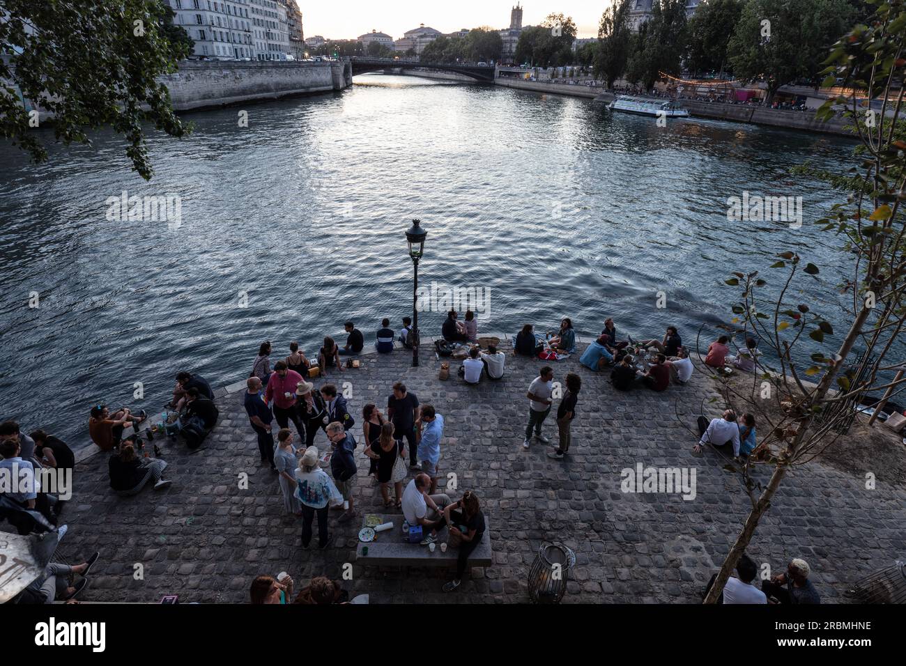 Romantic Paris. People at sunset on Right Bank of River Seine at Place Louis Aragon to socialise ...