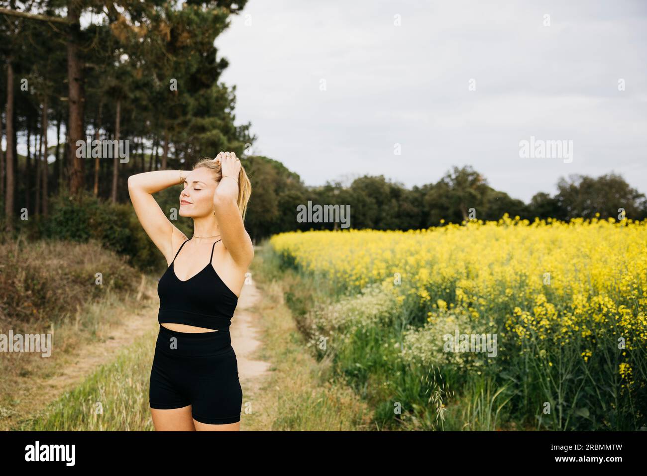 Young woman standing on next to a flower field and tying her hair ...
