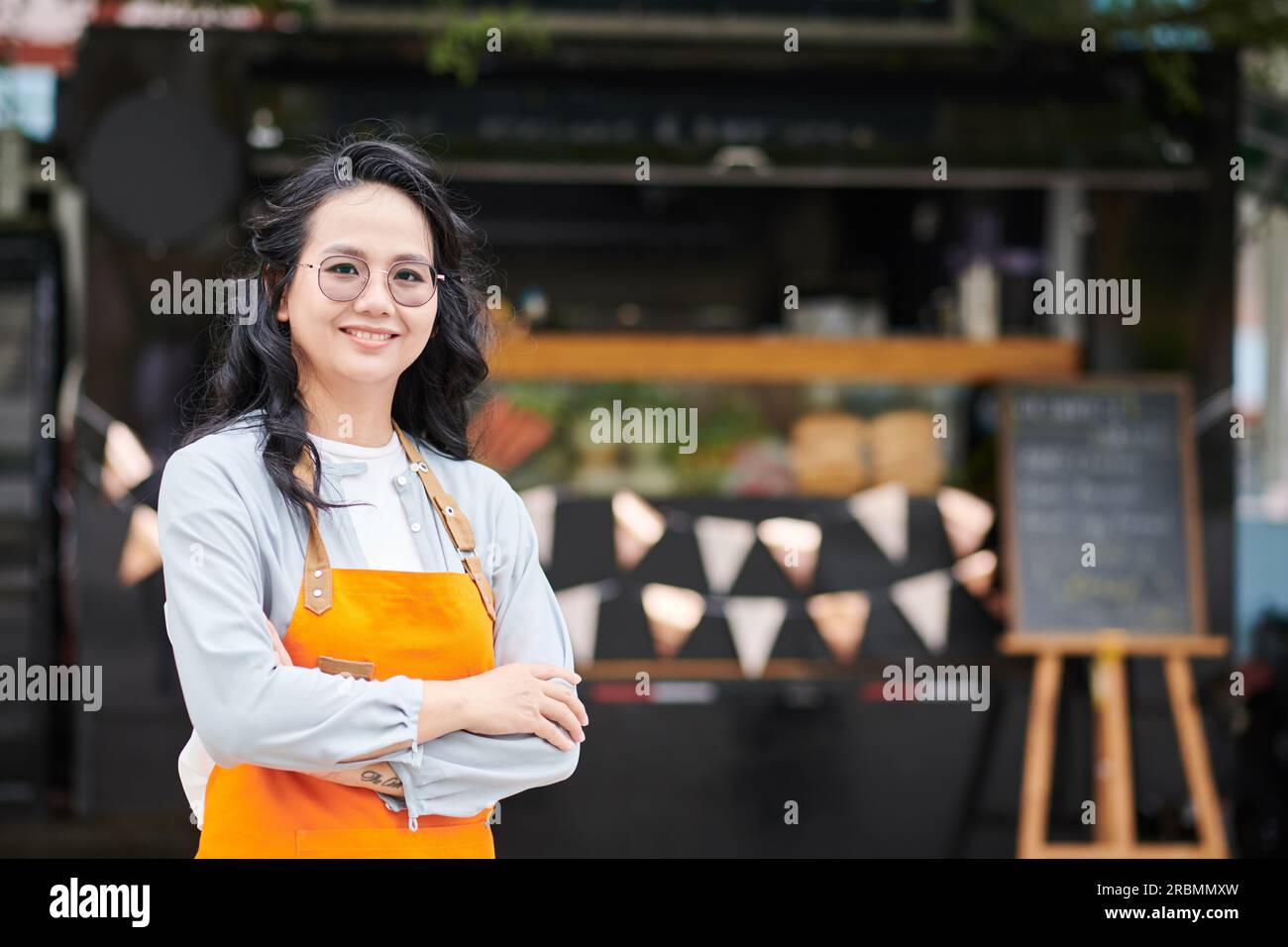 Portrait of smiling Vietnamese vendor in apron standing in front of her ...