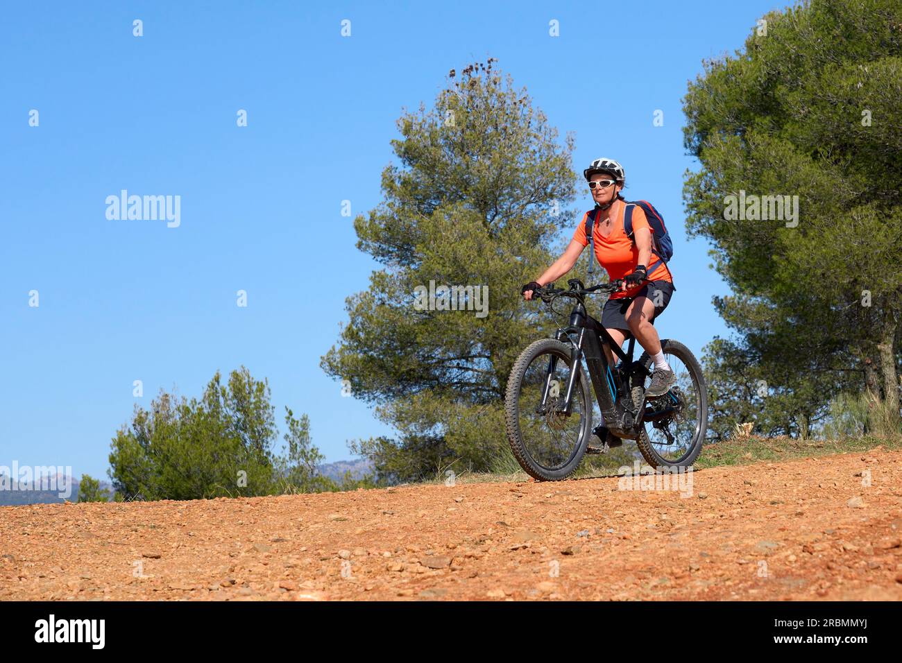 nice, active senior woman riding her electric mountain bike in the pine ...