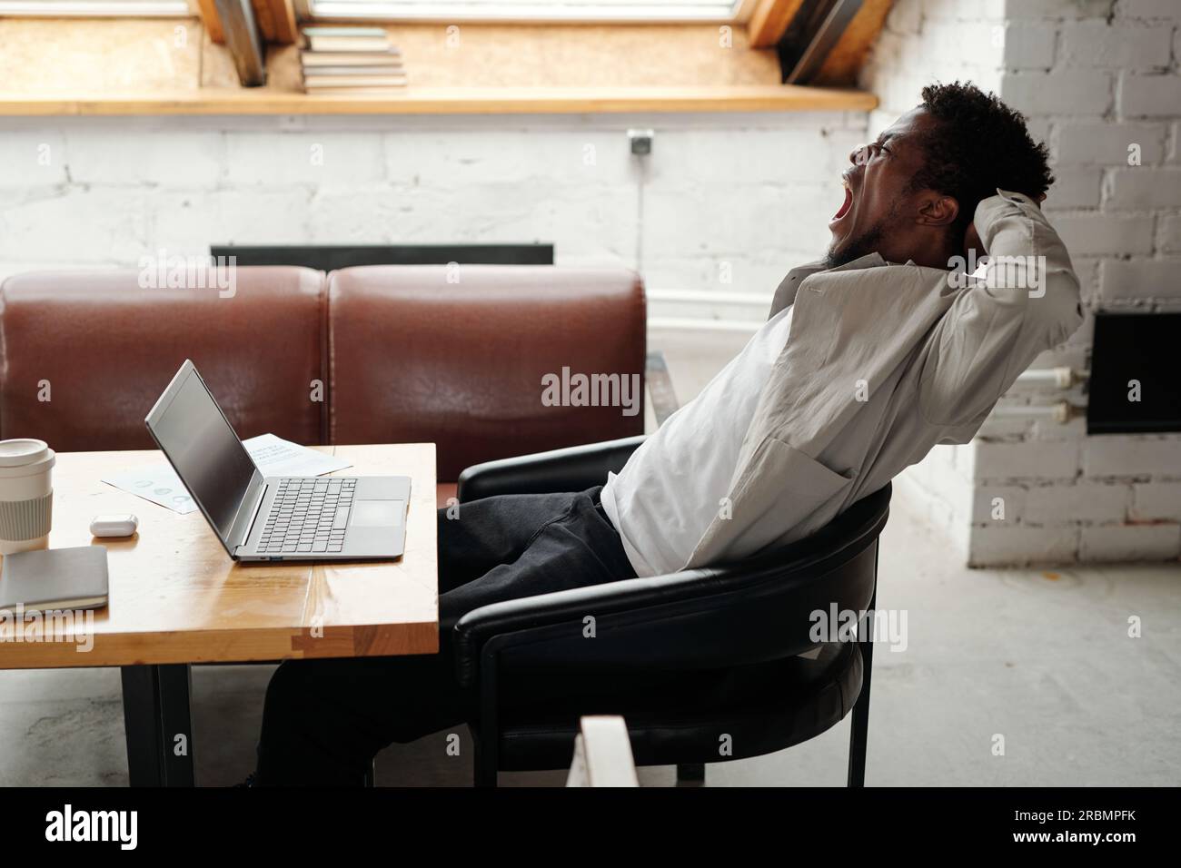 Side view of young yawning businessman with hands behind his head ...