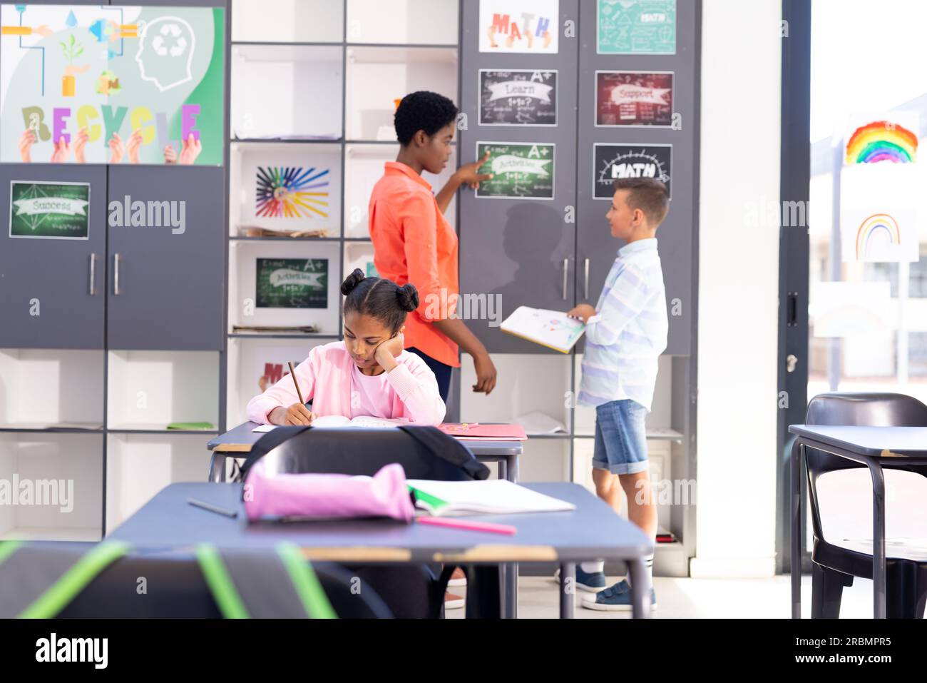 Diverse female teacher and schoolboy looking at posters and talking in ...