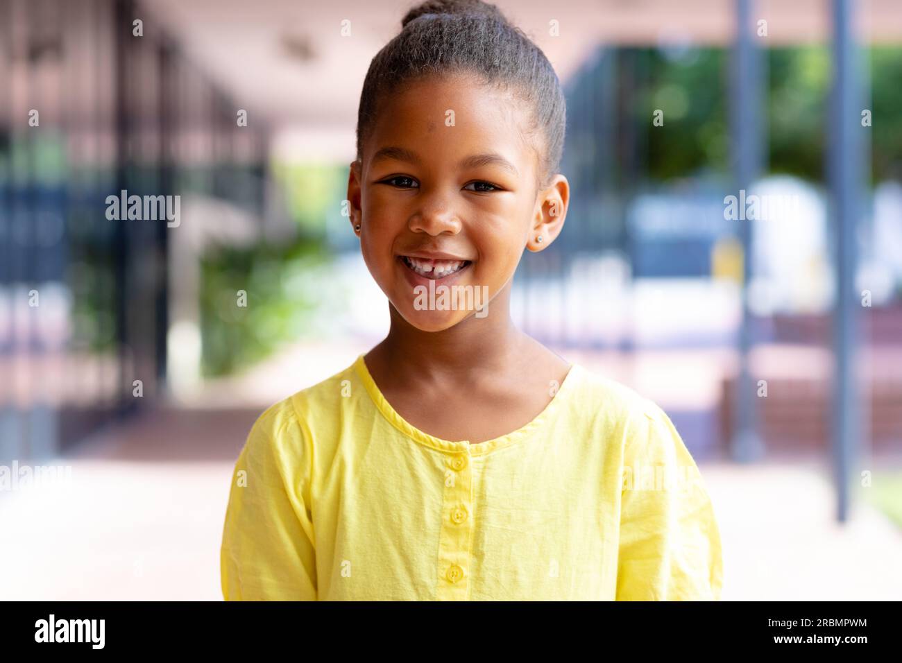Portrait of smiling biracial schoolgirl standing in sunny school corridor with copy space ...