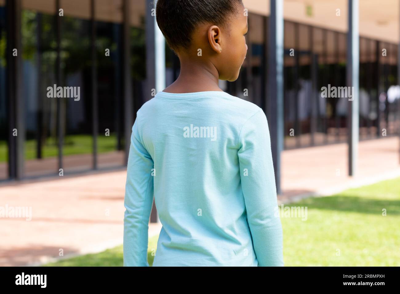 Rear view of biracial schoolgirl standing in sunny schoolyard ...