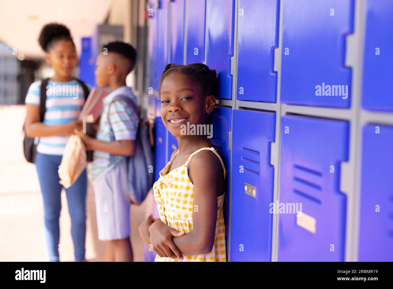 Portrait of happy african american schoolgirl standing next to locker ...