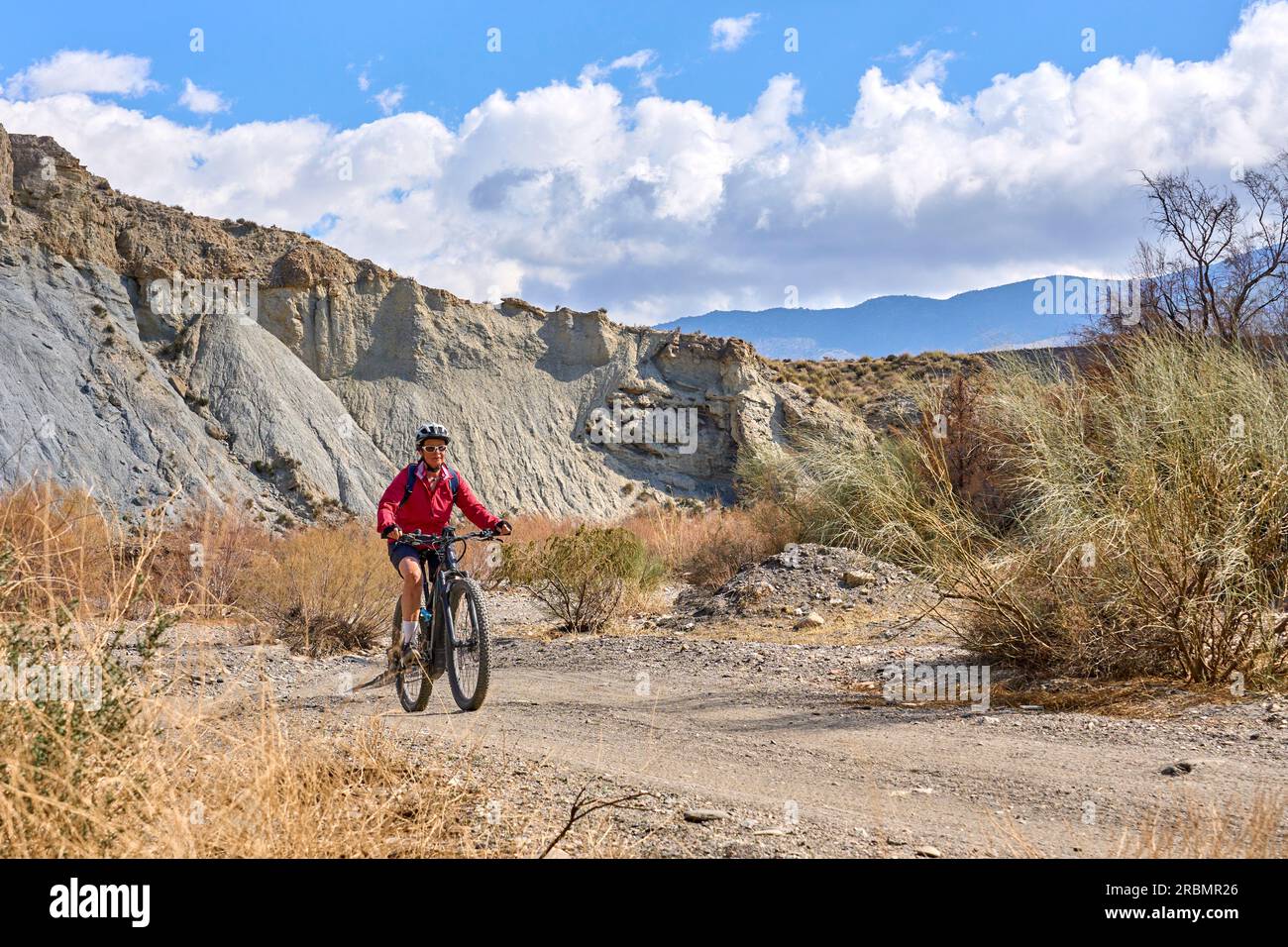 nice, active senior woman with her electric mountain bike on a trail tour in the desert of ...
