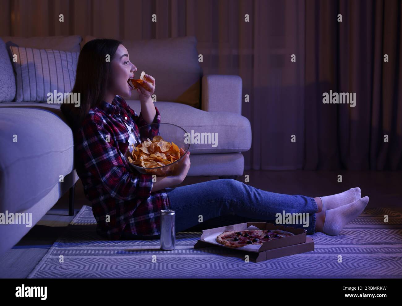 Young woman eating chips while watching TV in room at night. Bad habit Stock Photo - Alamy