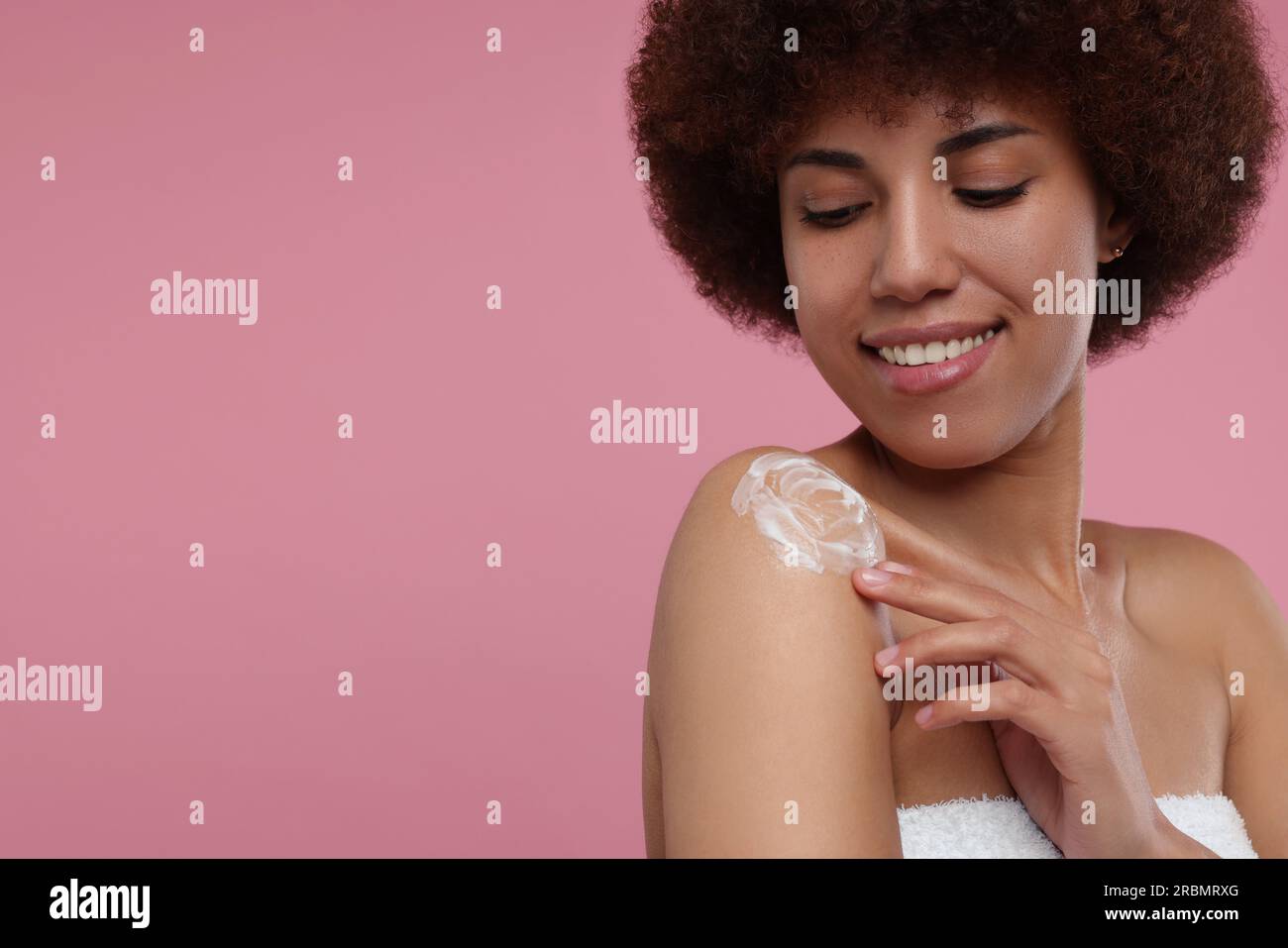 Beautiful young woman applying body cream onto shoulder on pink ...