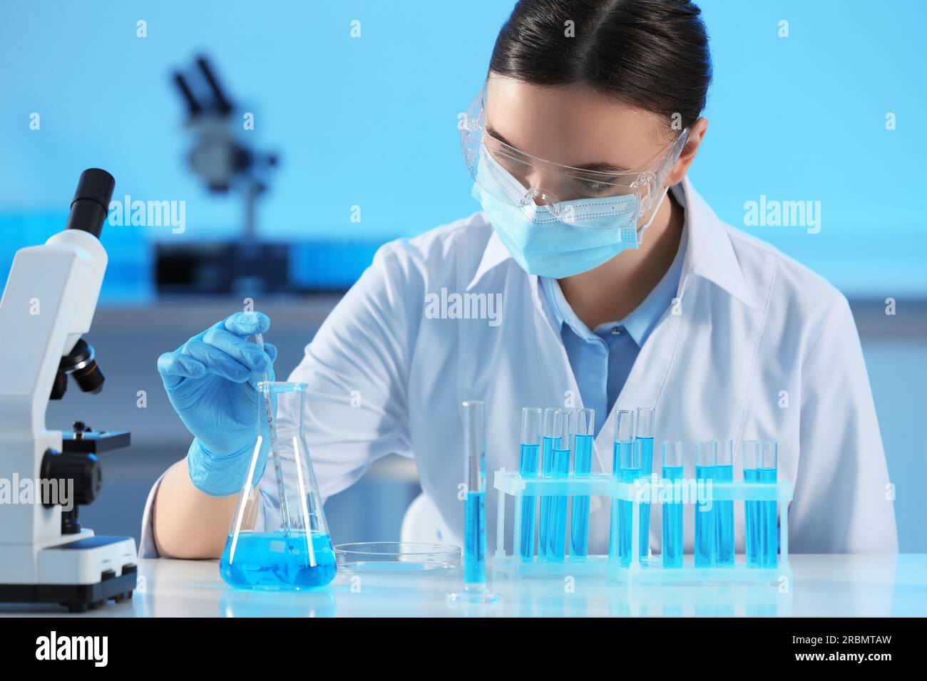Scientist taking sample of light blue liquid and test tubes in ...