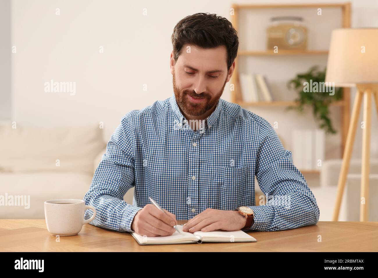 Happy man taking notes during video call at wooden desk indoors, view ...