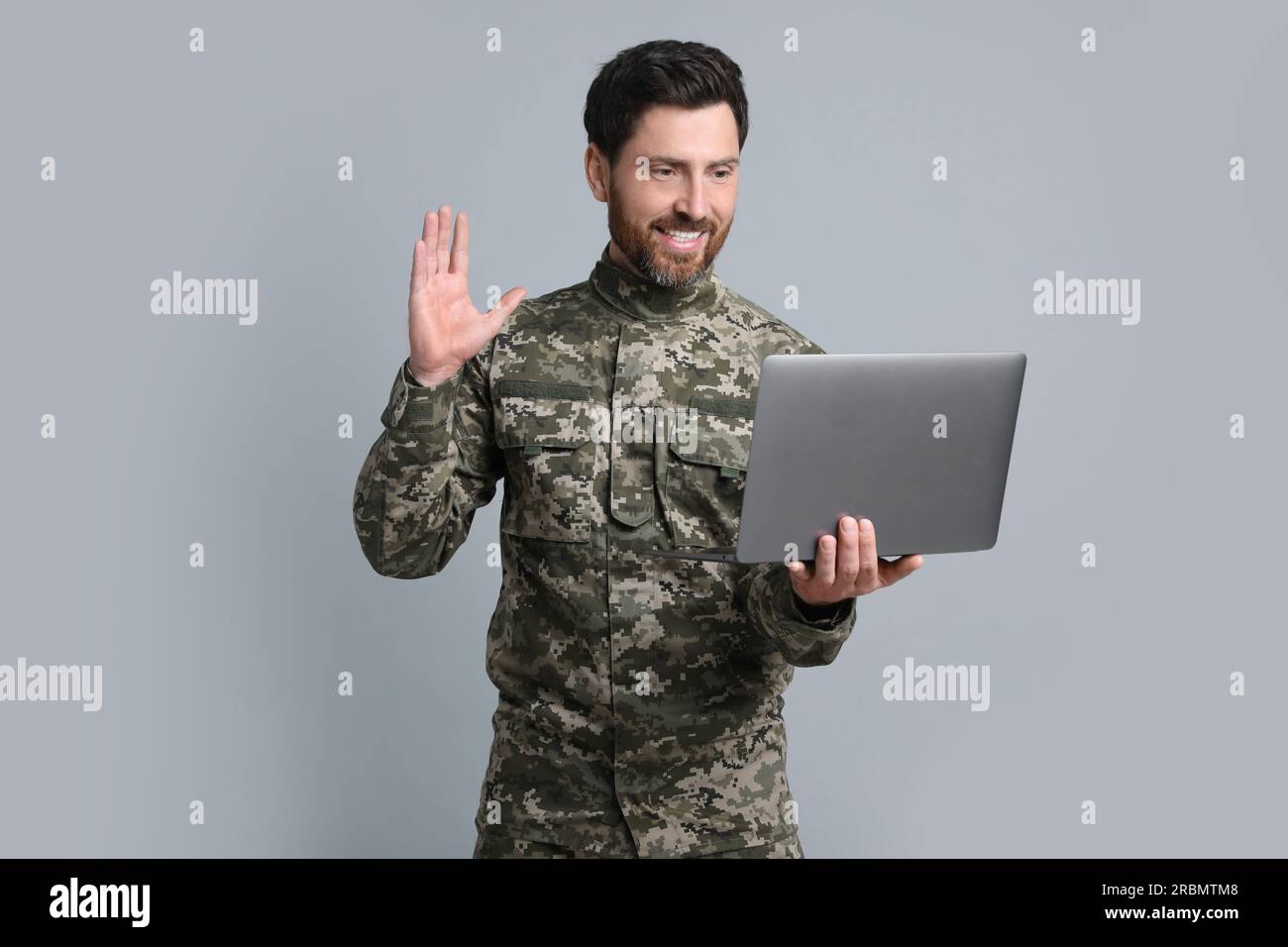 Happy soldier using video chat on laptop against light grey background ...