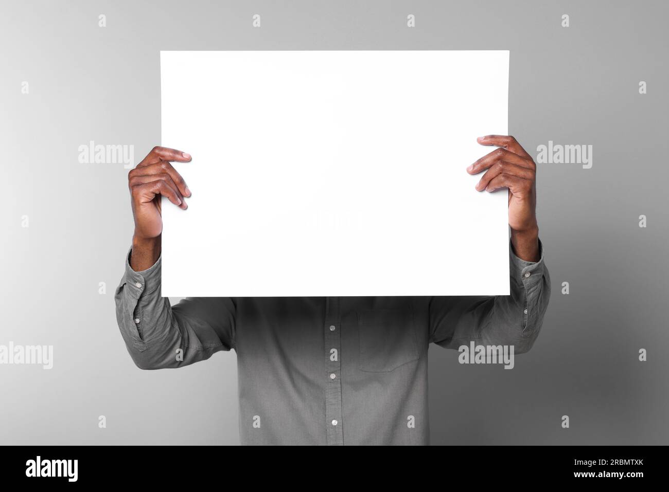 African American man holding sheet of paper on grey background. Mockup ...