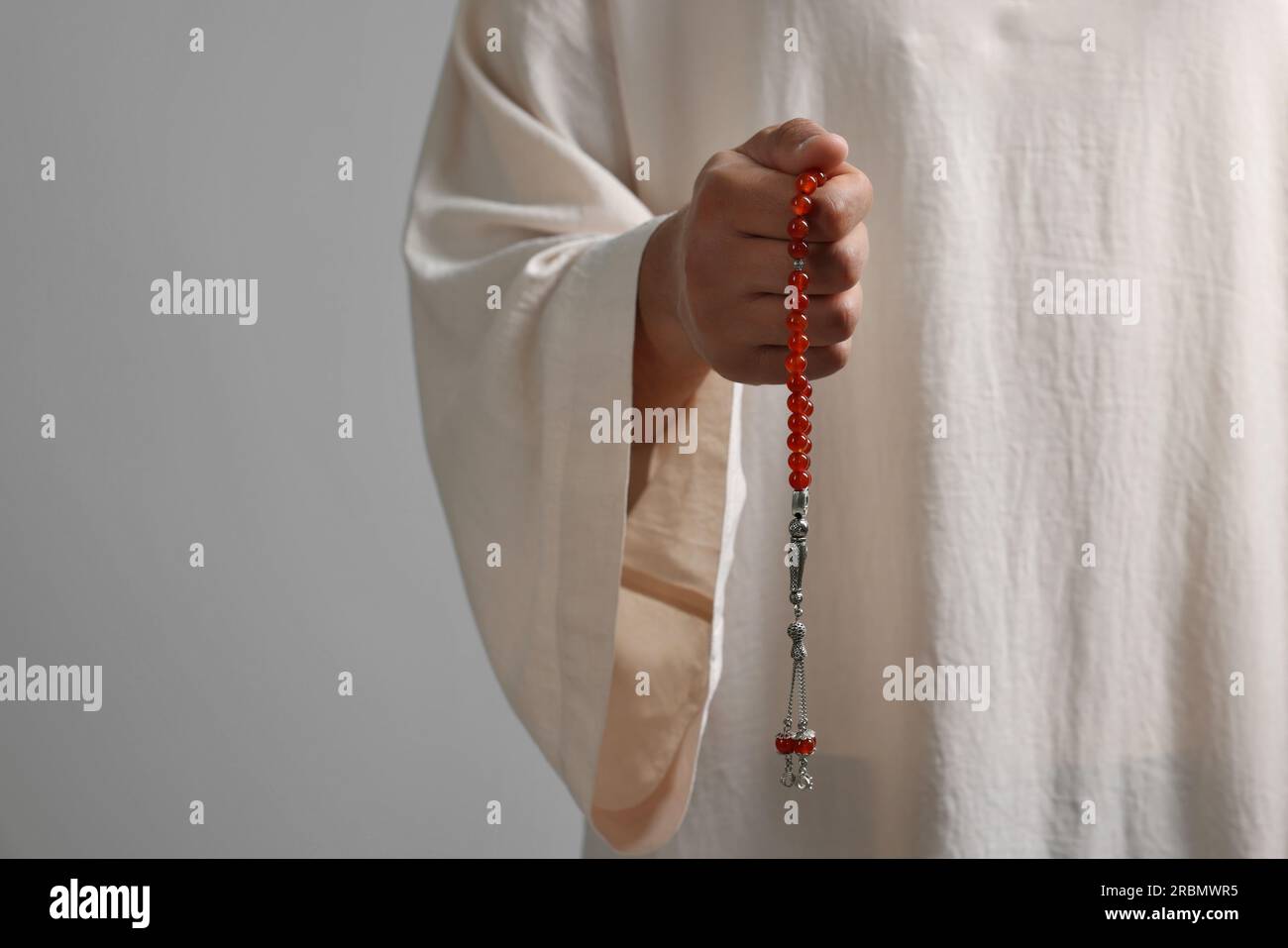 Muslim man with misbaha on light grey background, closeup. Space for ...