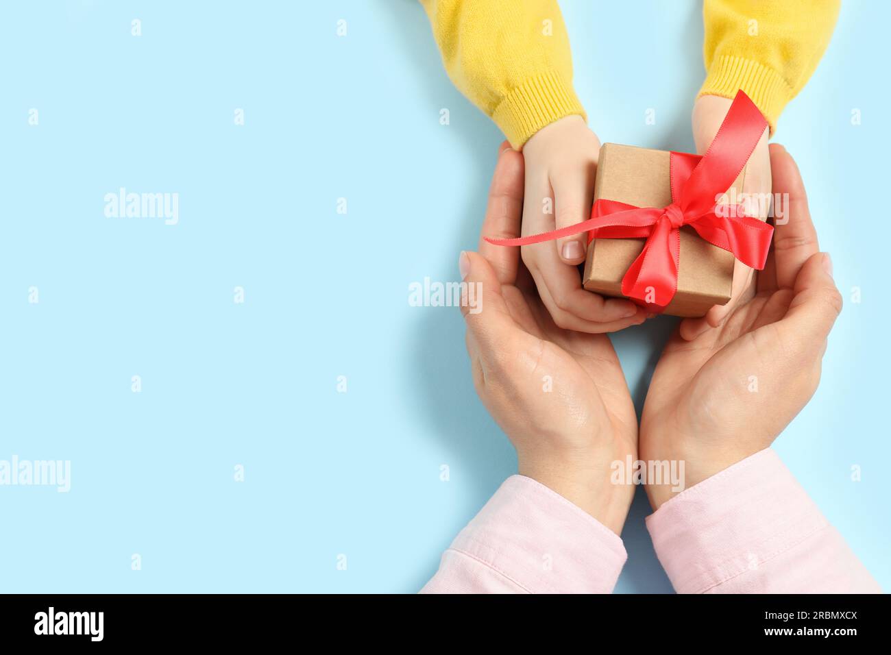 Mother giving gift box to her child on light blue background, top view ...