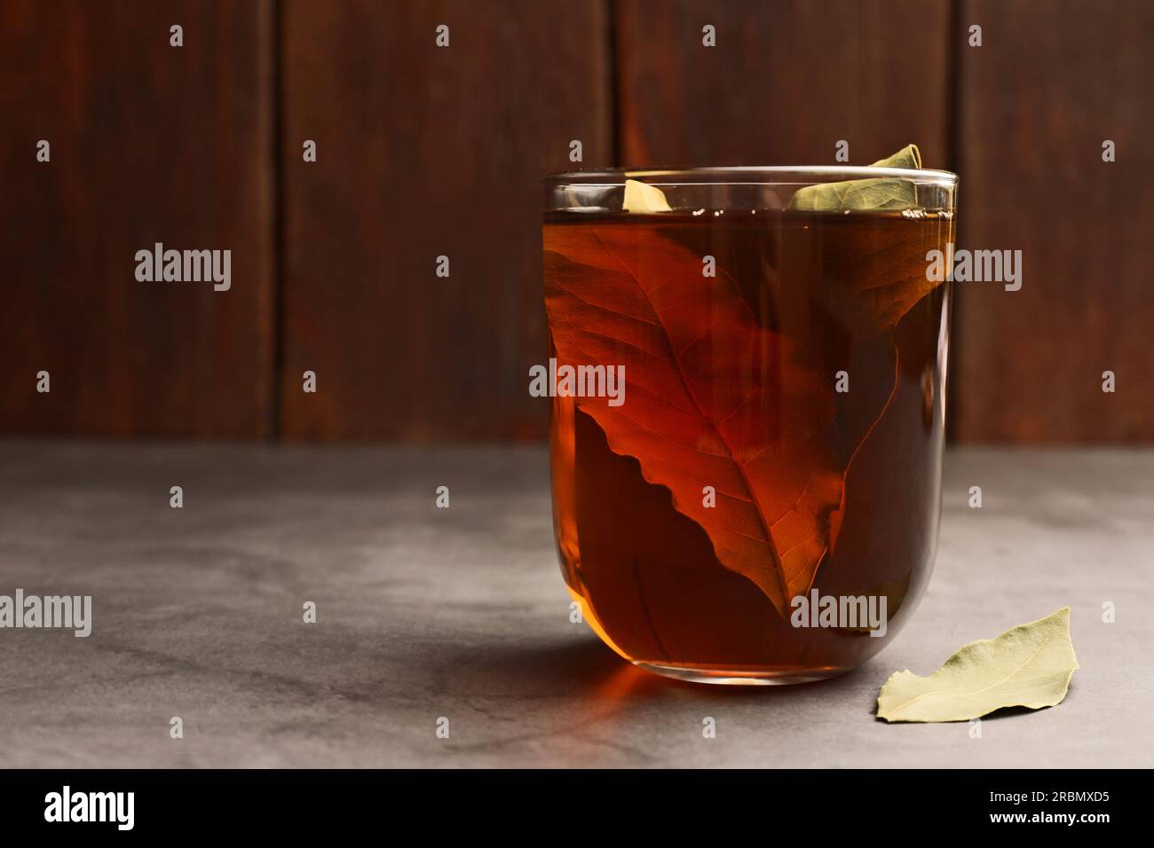 Cup of freshly brewed tea with bay leaves on grey table. Space for text ...