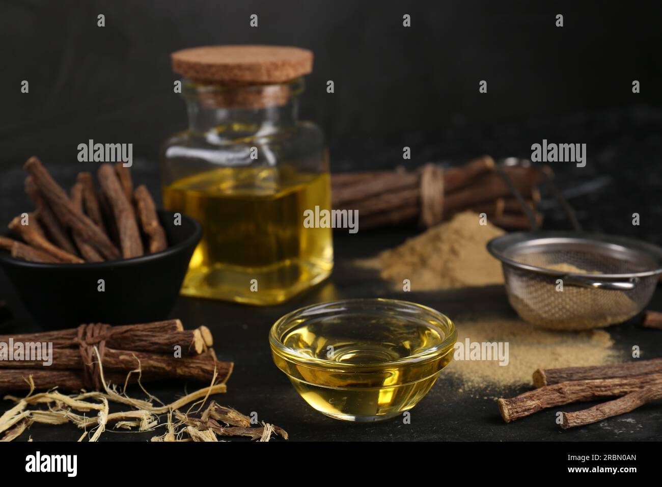 Dried sticks of licorice roots, powder and essential oil on black table ...
