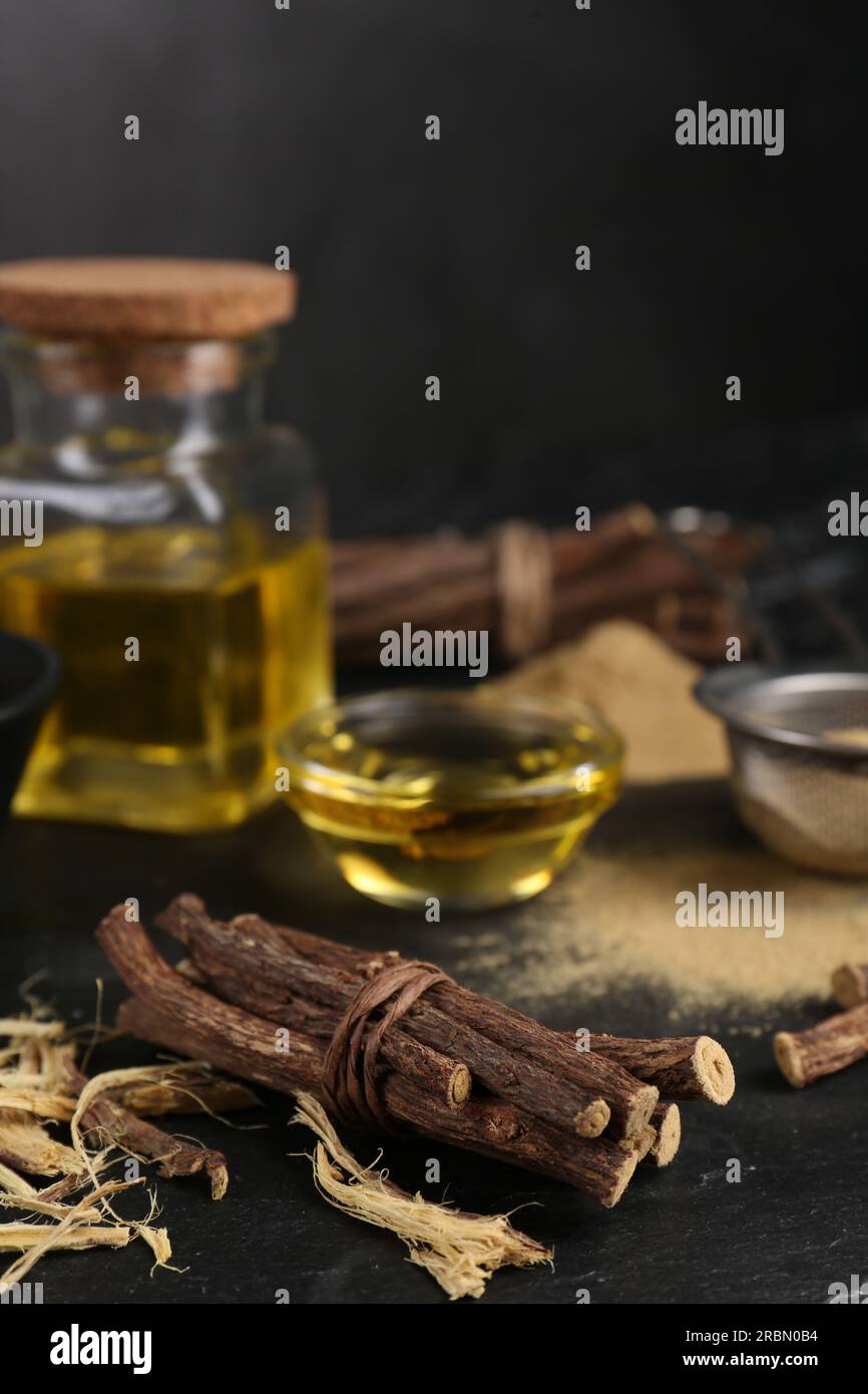 Dried sticks of licorice roots, powder and essential oil on black table ...