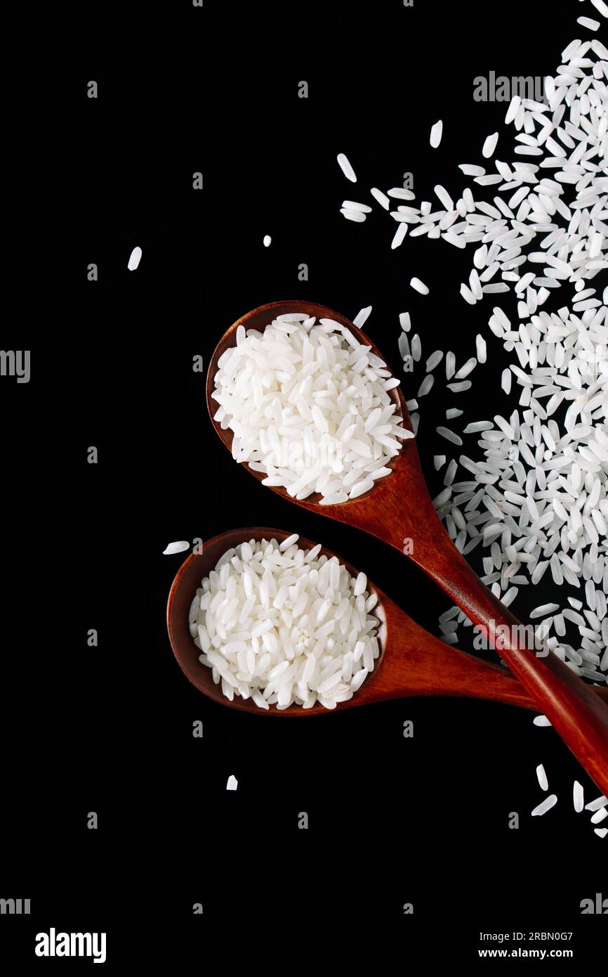 White long rice in wooden spoons on black background. Raw uncooked rice ...