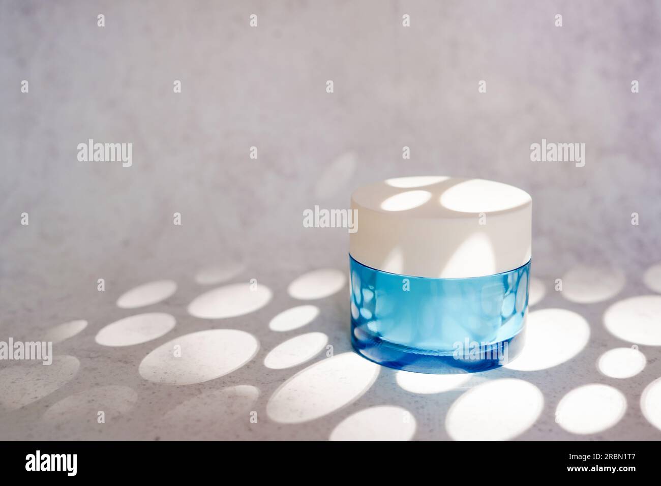 Blue glass moisturizer cream, shadows play on light concrete background ...