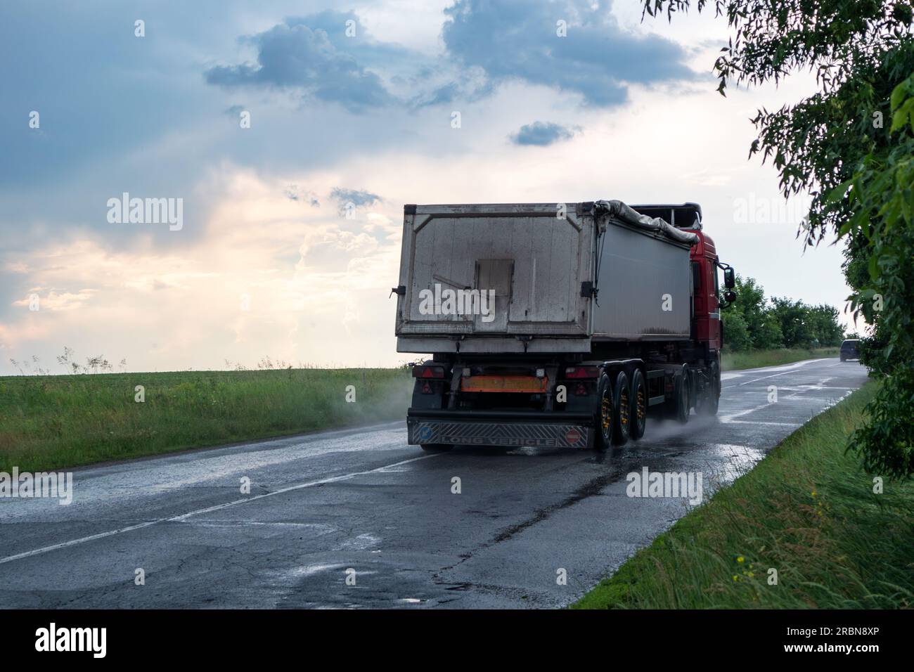 Heavy truck vehicle driving wet rural asphalt road driveway in stormy ...