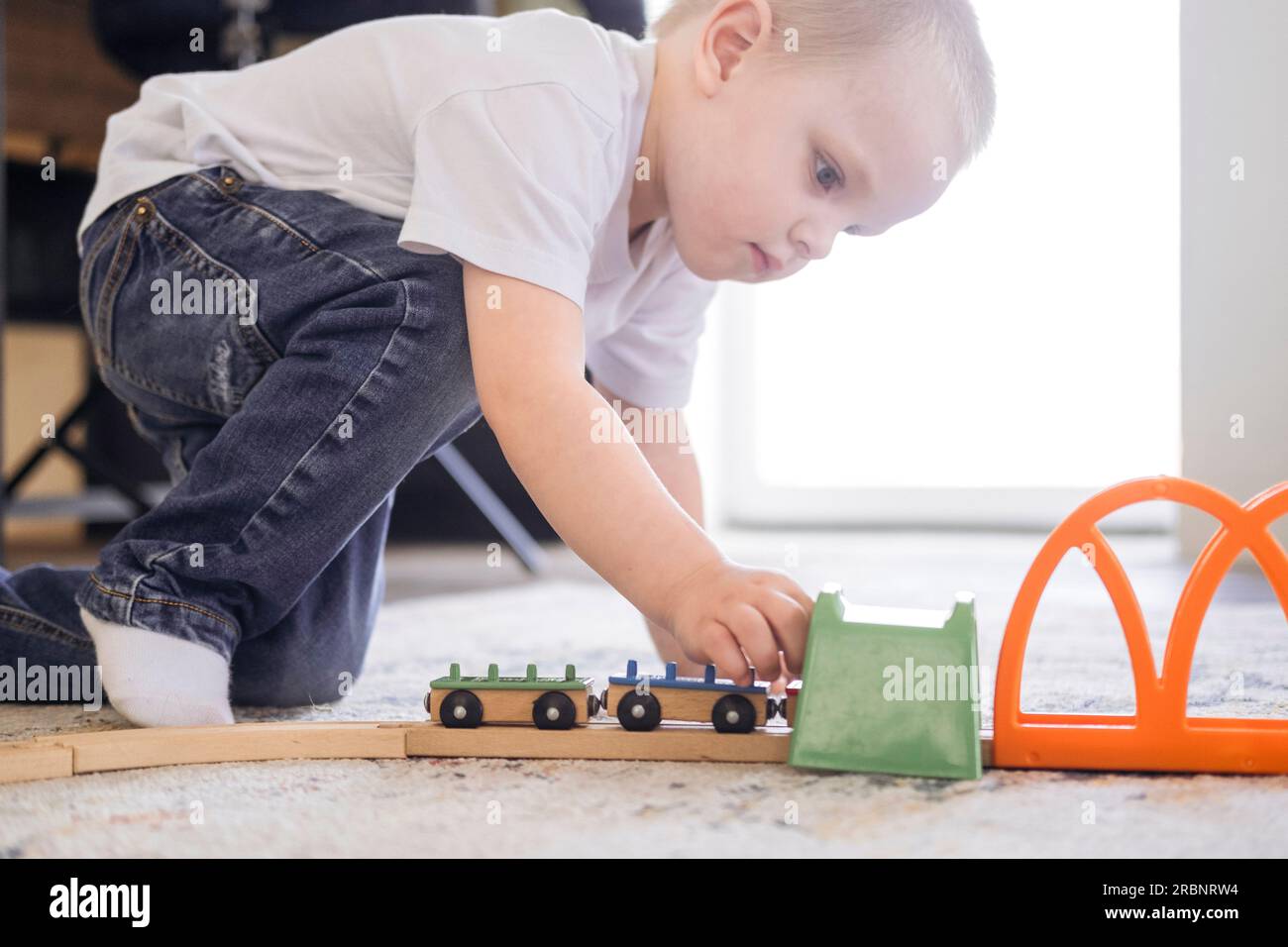 A little boy rides trains on the railroad at home on the floor. The kid ...