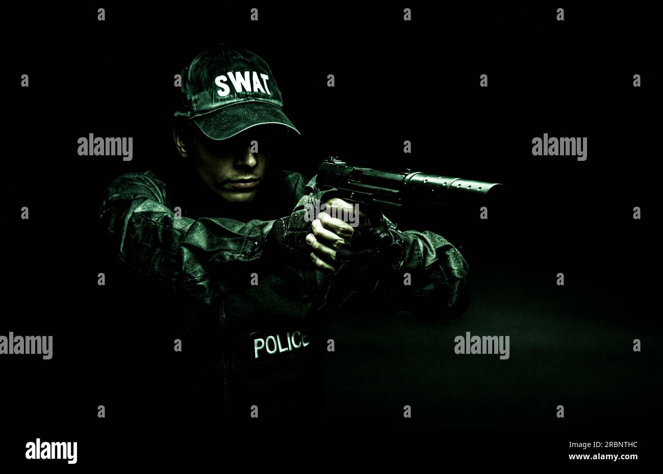 Spec ops police officer SWAT in black uniform aiming pistol with silencer, studio shot, half ...