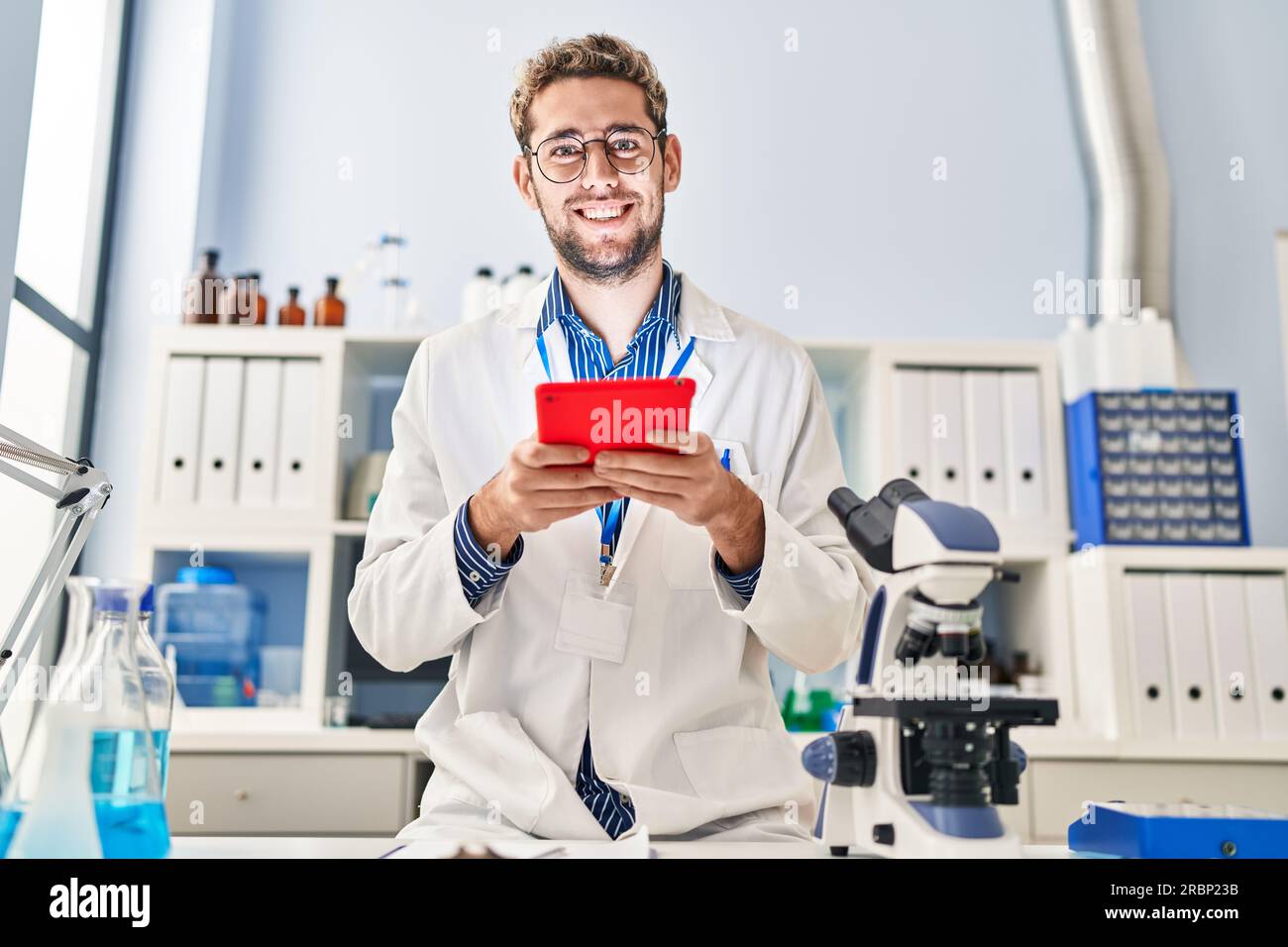 Young man scientist smiling confident using touchpad at laboratory ...