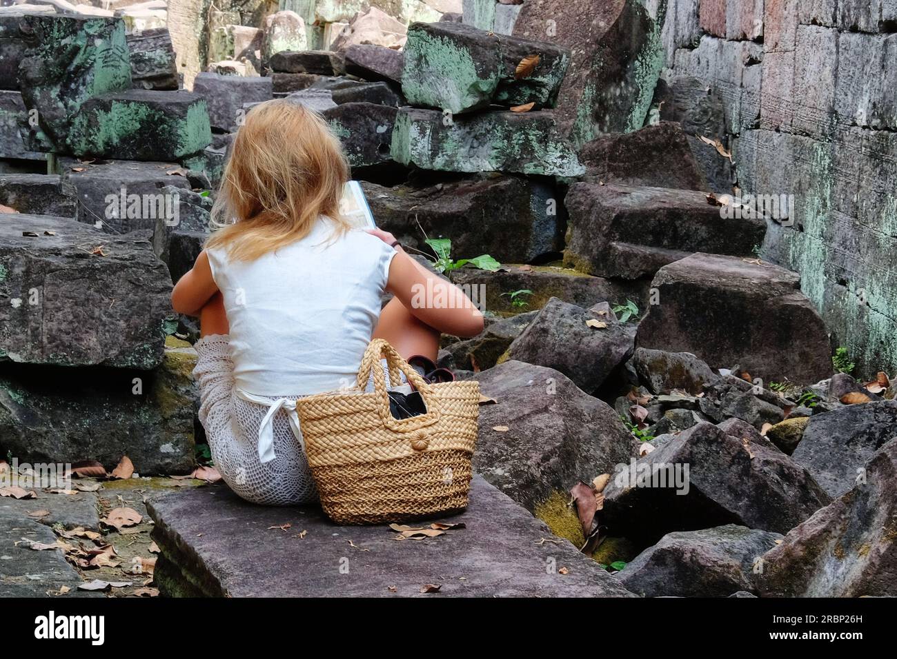 A young blonde European girl is sitting on a stone among medieval ruins ...