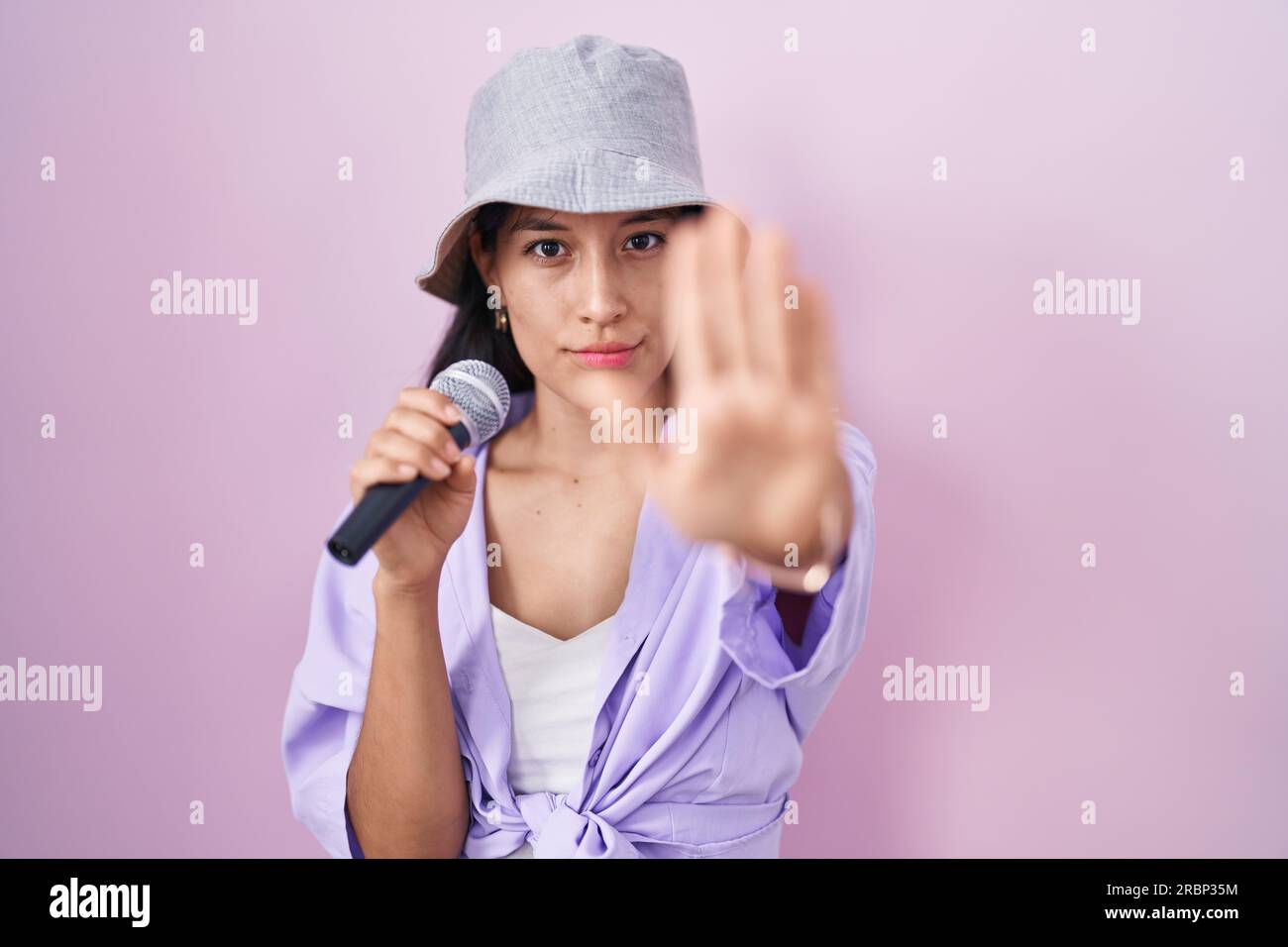 Young hispanic woman singing song using microphone over pink background ...