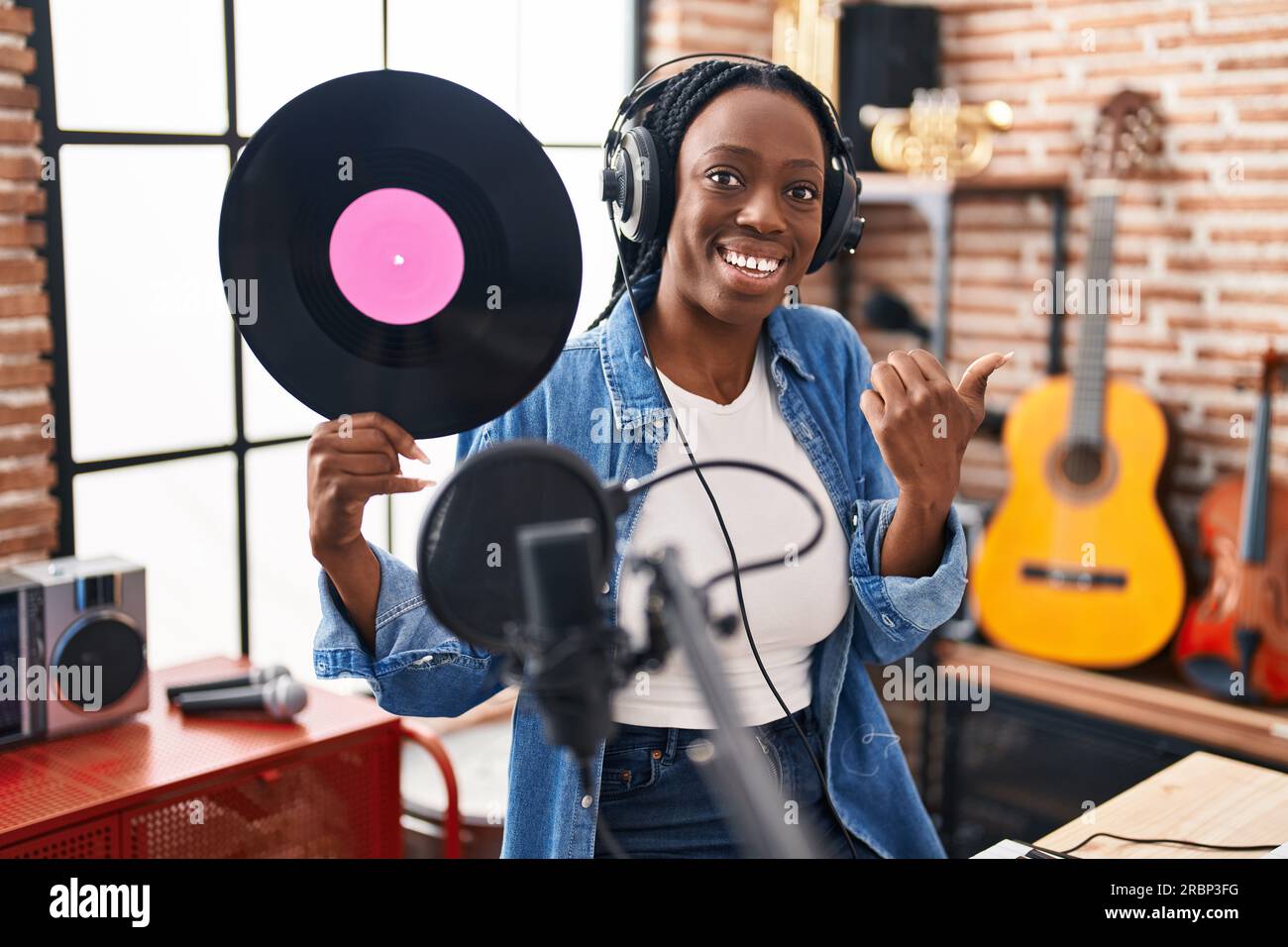 Beautiful black woman holding vinyl record at music studio pointing ...