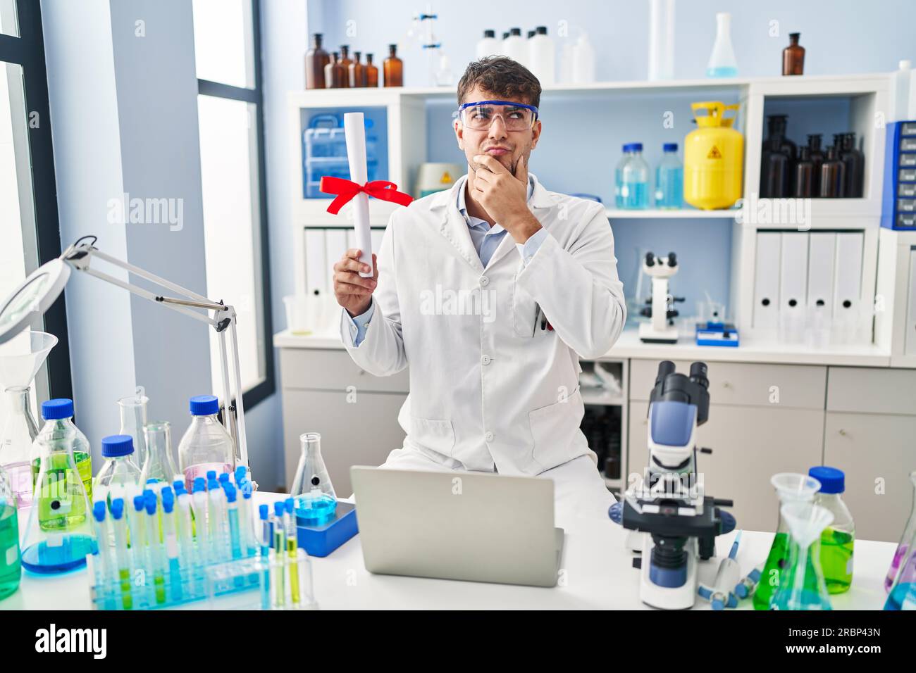 Young hispanic man working at scientist laboratory holding diploma ...
