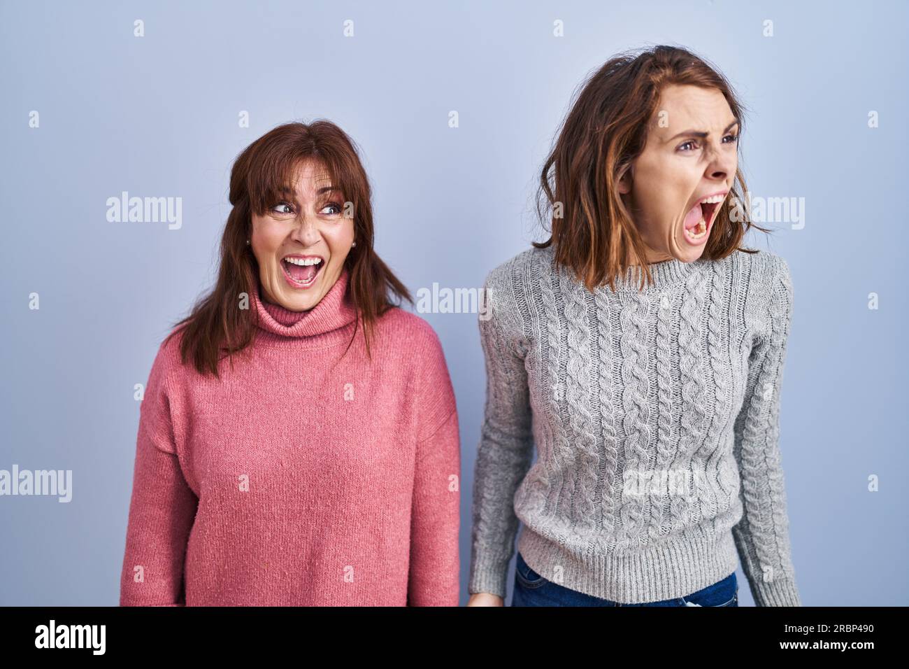 Mother and daughter standing over blue background angry and mad ...