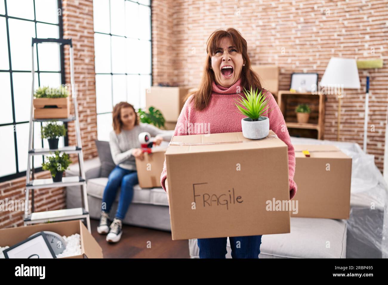 Mother and daughter moving to a new home holding cardboard box angry ...