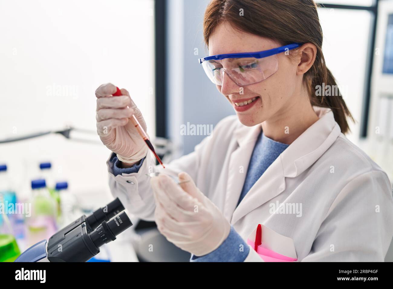Young blonde woman scientist pouring blood on sample at laboratory ...