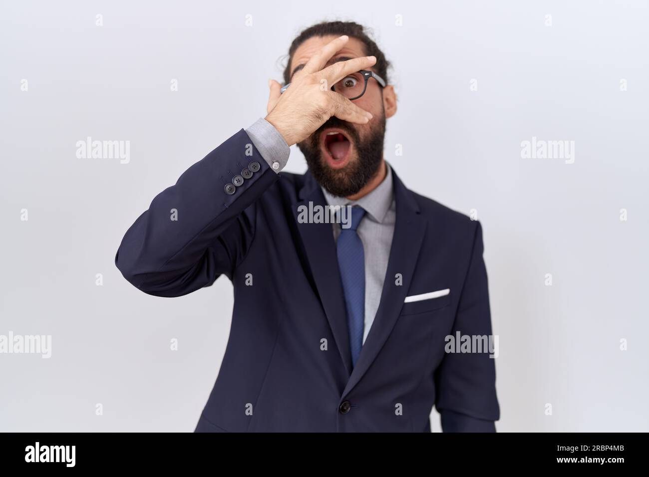 Hispanic man with beard wearing suit and tie peeking in shock covering ...